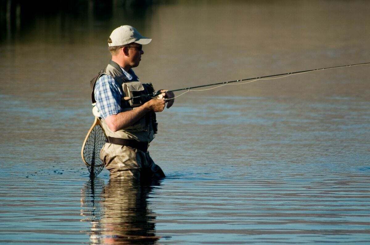 Uma pessoa de pé na água, segurando uma vara de pesca.