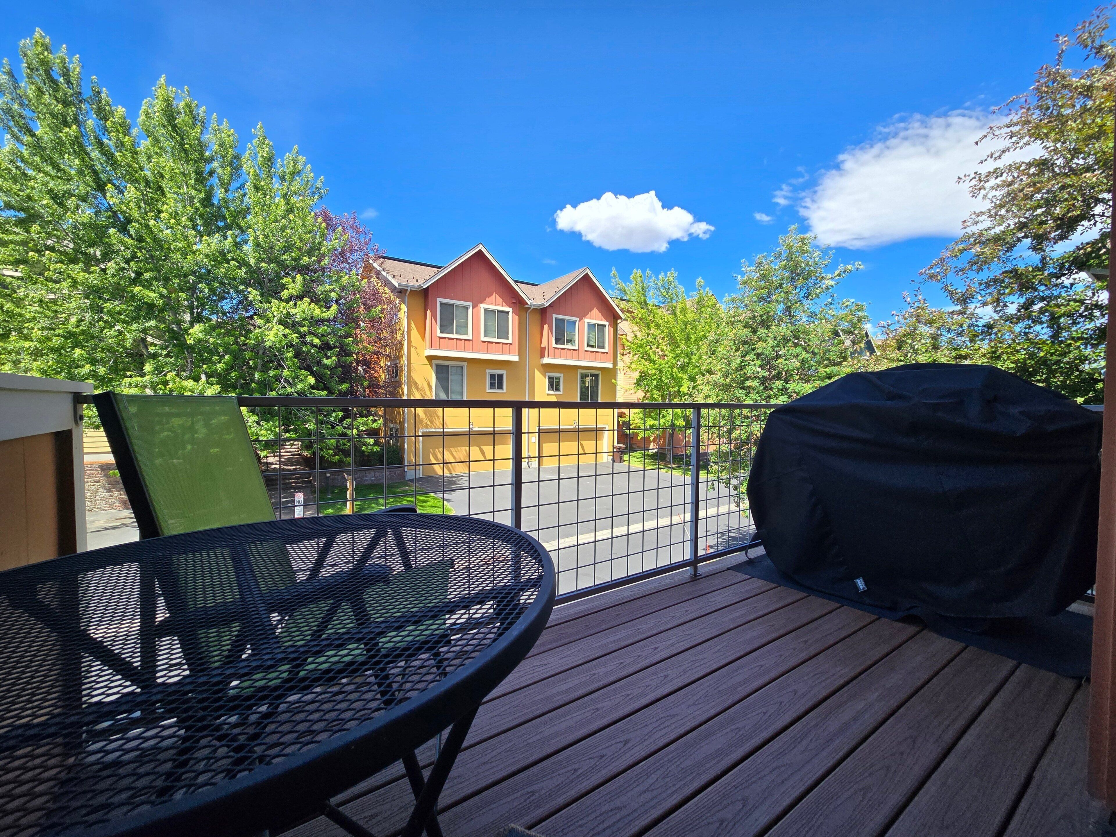Um terraço com uma mesa de metal e churrasqueira, com vista para uma área residencial com casas coloridas.