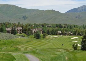 Um campo de golfe com vários edifícios, uma estrada sinuosa e colinas circundantes.