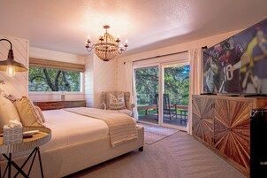 Quarto com uma cama grande, um candelabro, televisão e uma porta de vidro deslizante que dá para uma varanda.