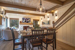 Uma sala de jantar com mesa e cadeiras de madeira, um candelabro e uma escada que leva a um andar superior.