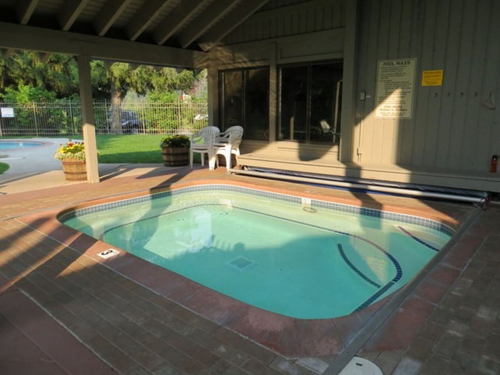 Piscina coberta com borda azulejada, área de estar com cadeiras e uma cerca ao fundo.