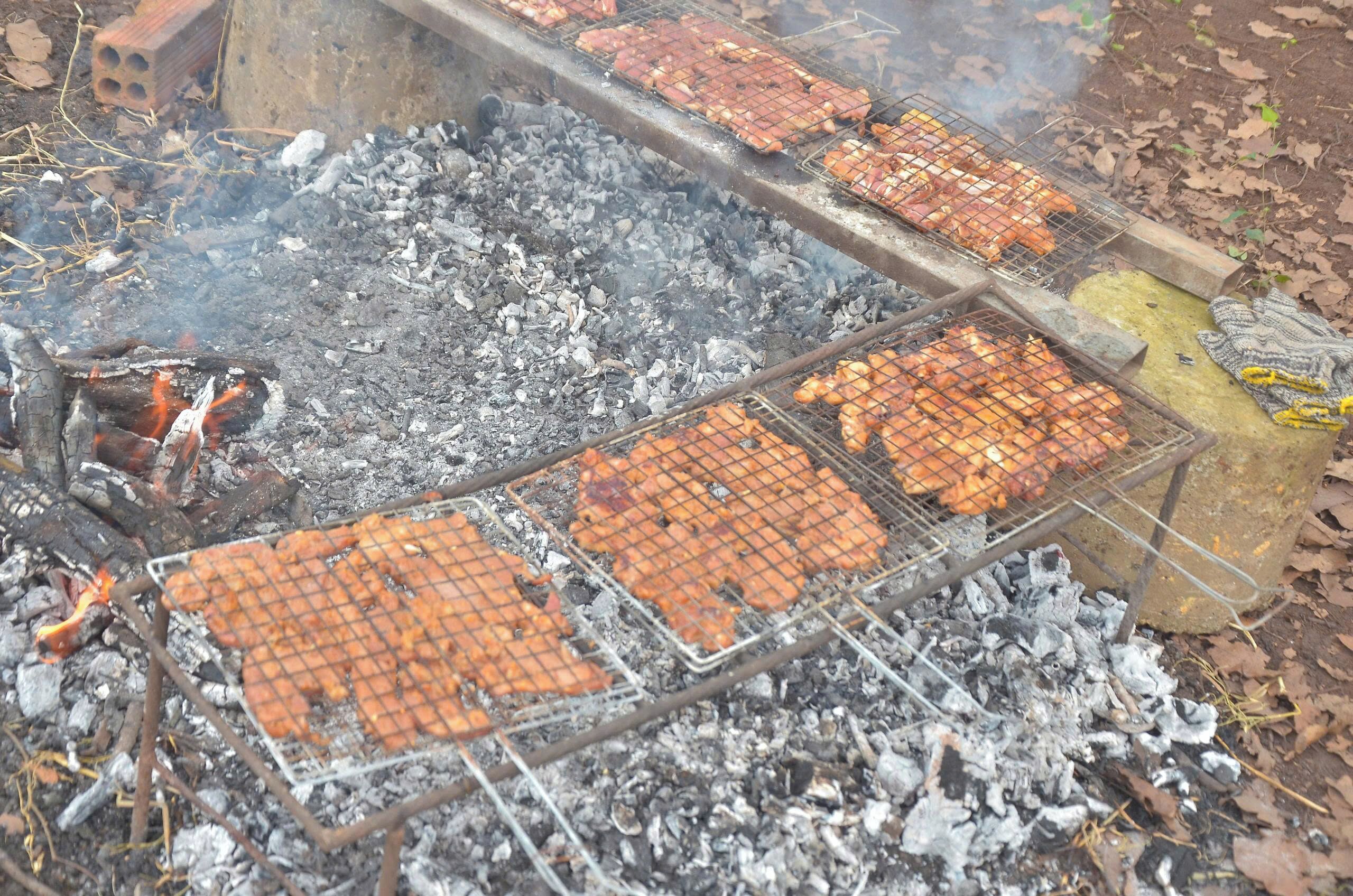 Uma churrasqueira com várias grelhas sobre carvão, em meio a um ambiente natural.