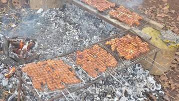 Uma churrasqueira com várias grelhas sobre carvão, em meio a um ambiente natural.