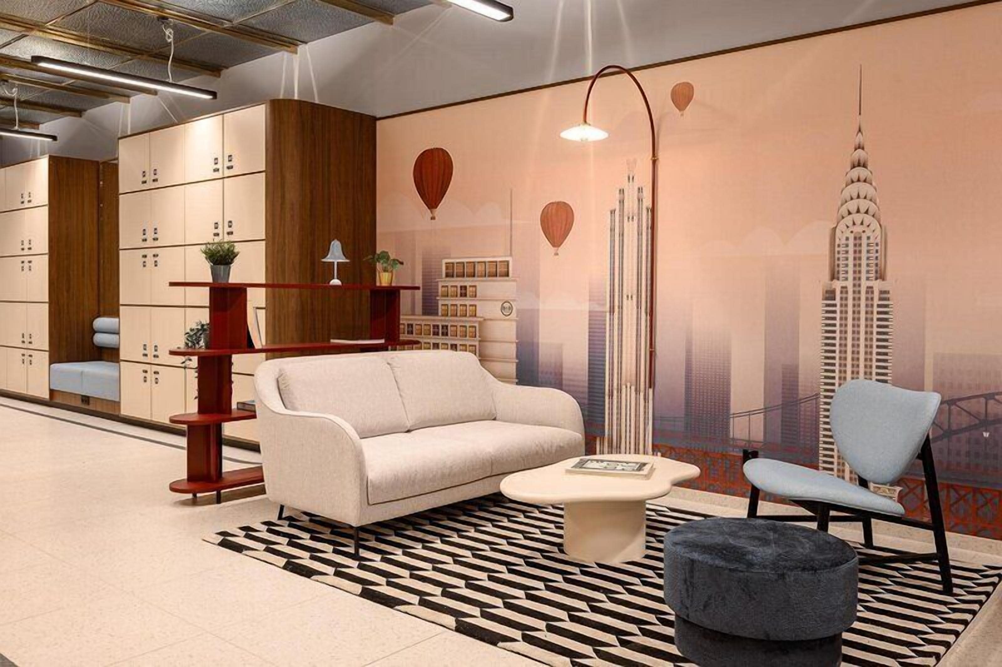 Um interior moderno com sofá, mesa de centro e banquinho, armários de madeira e um mural com prédios da cidade.