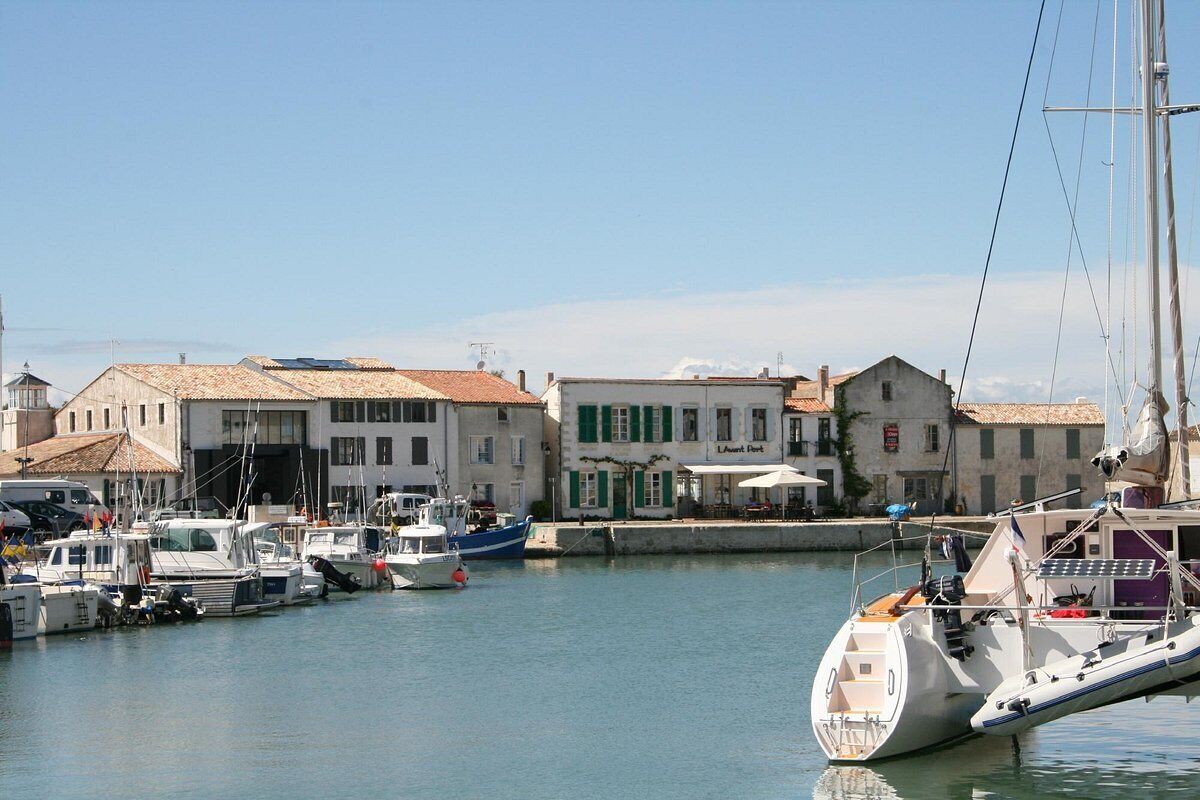 Uma marina com barcos atracados, um edifício com a placa 'L'Assiette Port' e um céu claro.