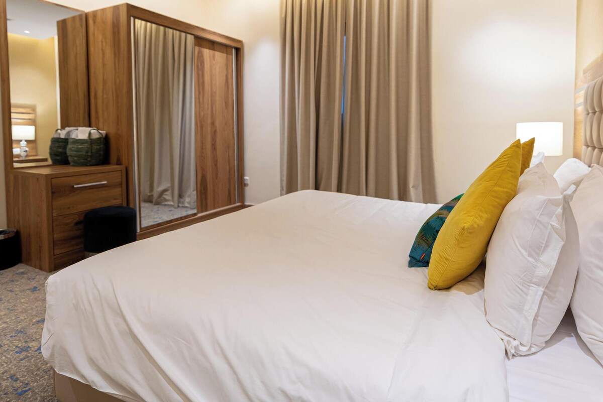 Quarto de hotel com uma cama grande, um guarda-roupa de madeira, um espelho e uma janela com cortinas.