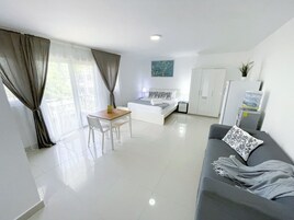 Quarto moderno e bem iluminado com cama, uma mesinha com cadeiras, sofá e frigorífico.
