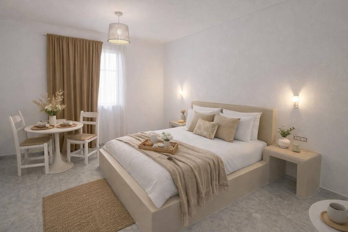 Quarto com cama, mesas de cabeceira, uma cadeira, uma mesinha e uma janela com cortinas.