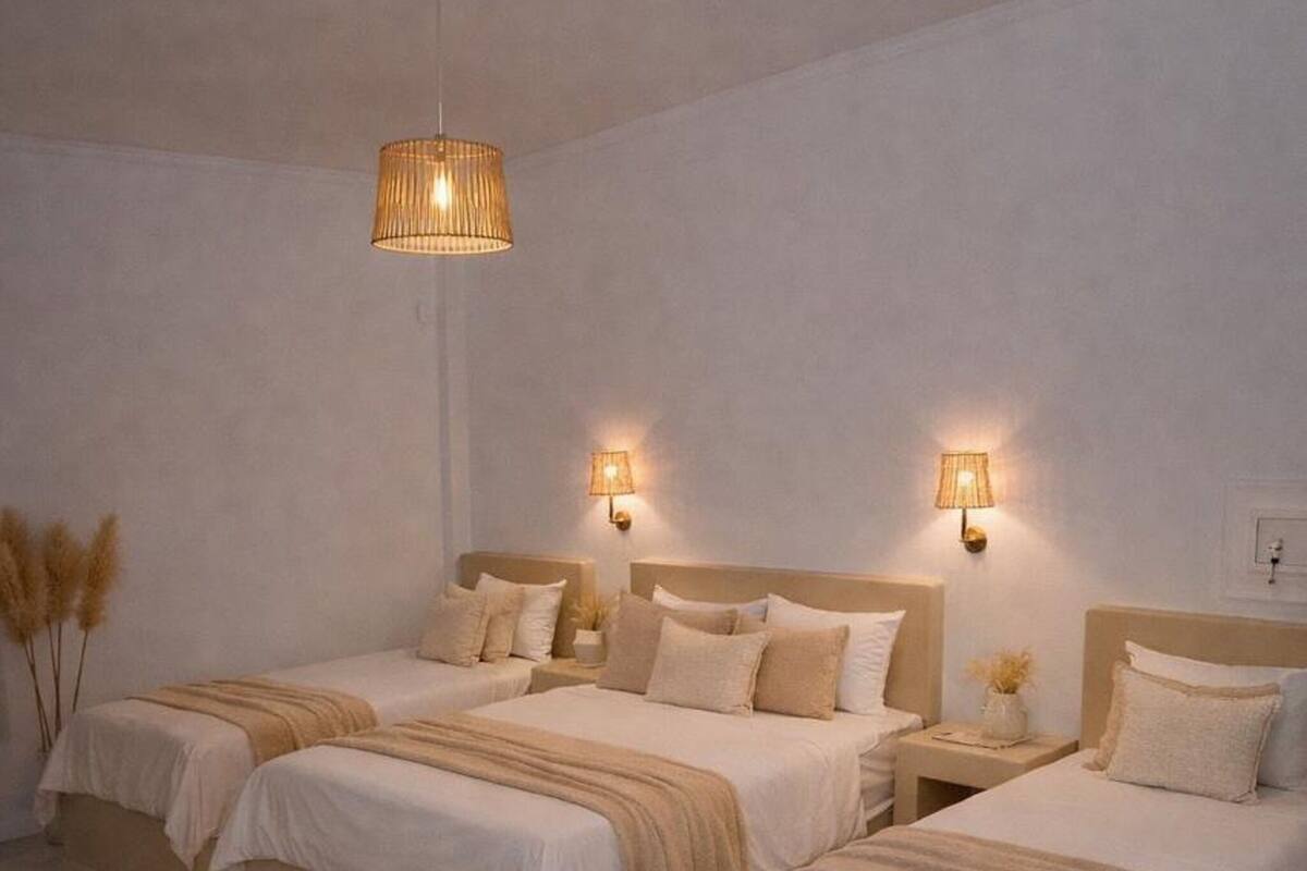 Quarto com duas camas, luminária pendente, arandelas e tapete de palha.