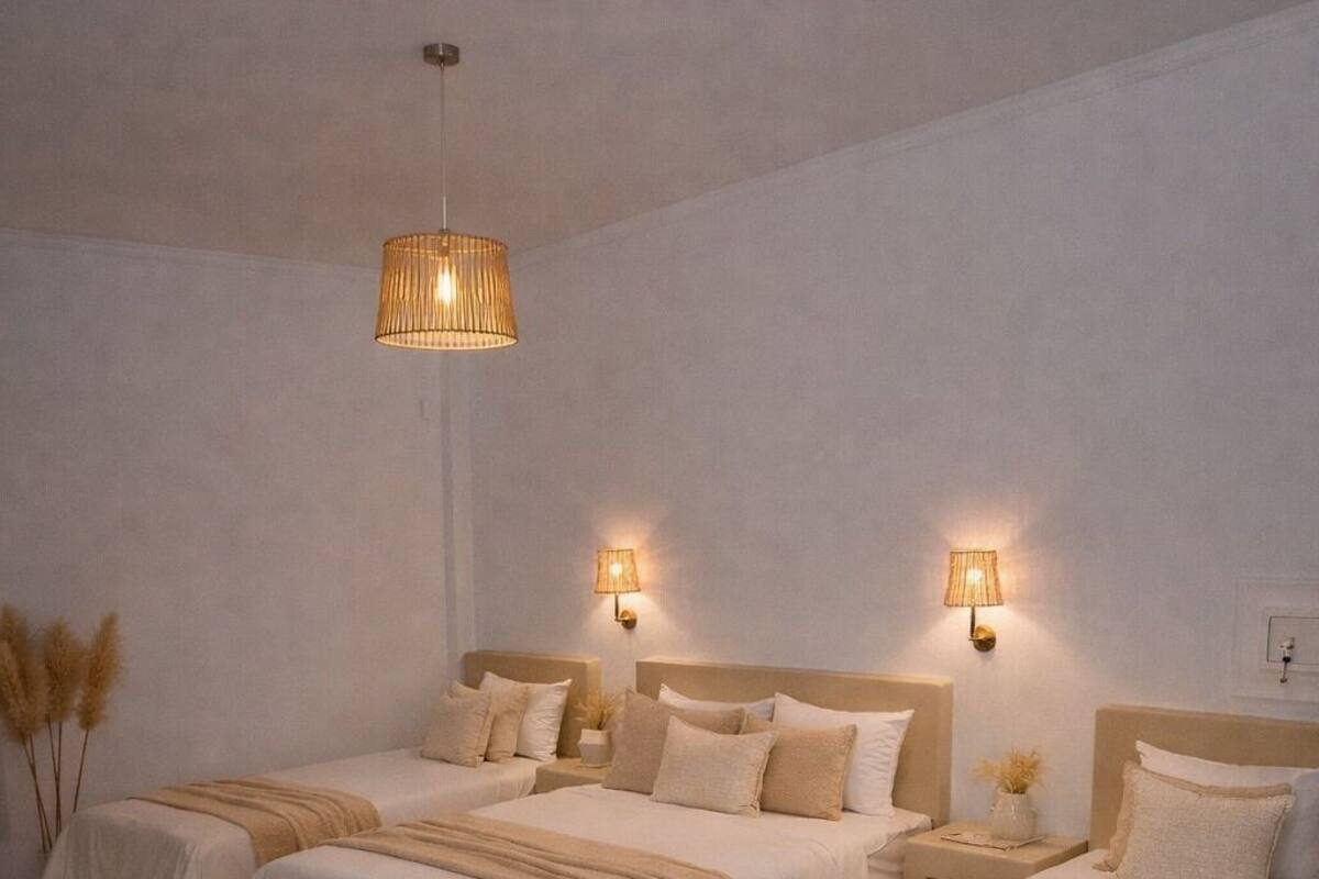 Quarto com duas camas, luminária pendente, luminárias na parede e plantas decorativas.