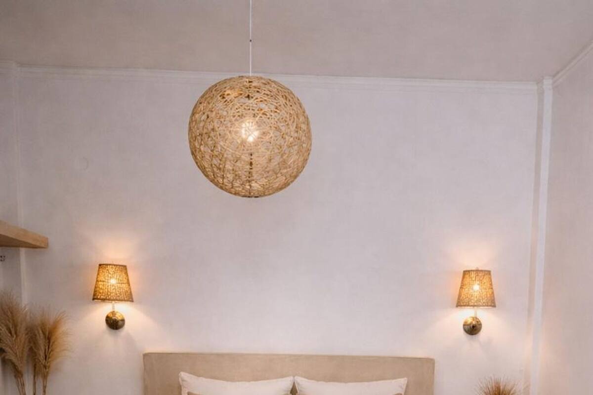 Quarto com cama grande, duas mesas de cabeceira, luminária pendente e tapete texturizado.