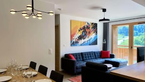Uma área de jantar com uma mesa posta para seis pessoas, um sofá preto com almofadas vermelhas e um quadro abstrato colorido na parede.