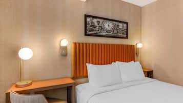 Quarto de hotel com cama, escrivaninha, cadeira e duas luminárias fixadas na parede.