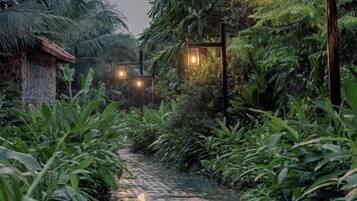 Um canal estreito ladeado por vegetação exuberante e construções tradicionais com telhados de palha, iluminado por iluminação suave.
