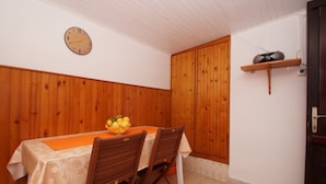 Uma sala de jantar com uma mesa posta para dois, um relógio na parede e um rádio em uma prateleira.