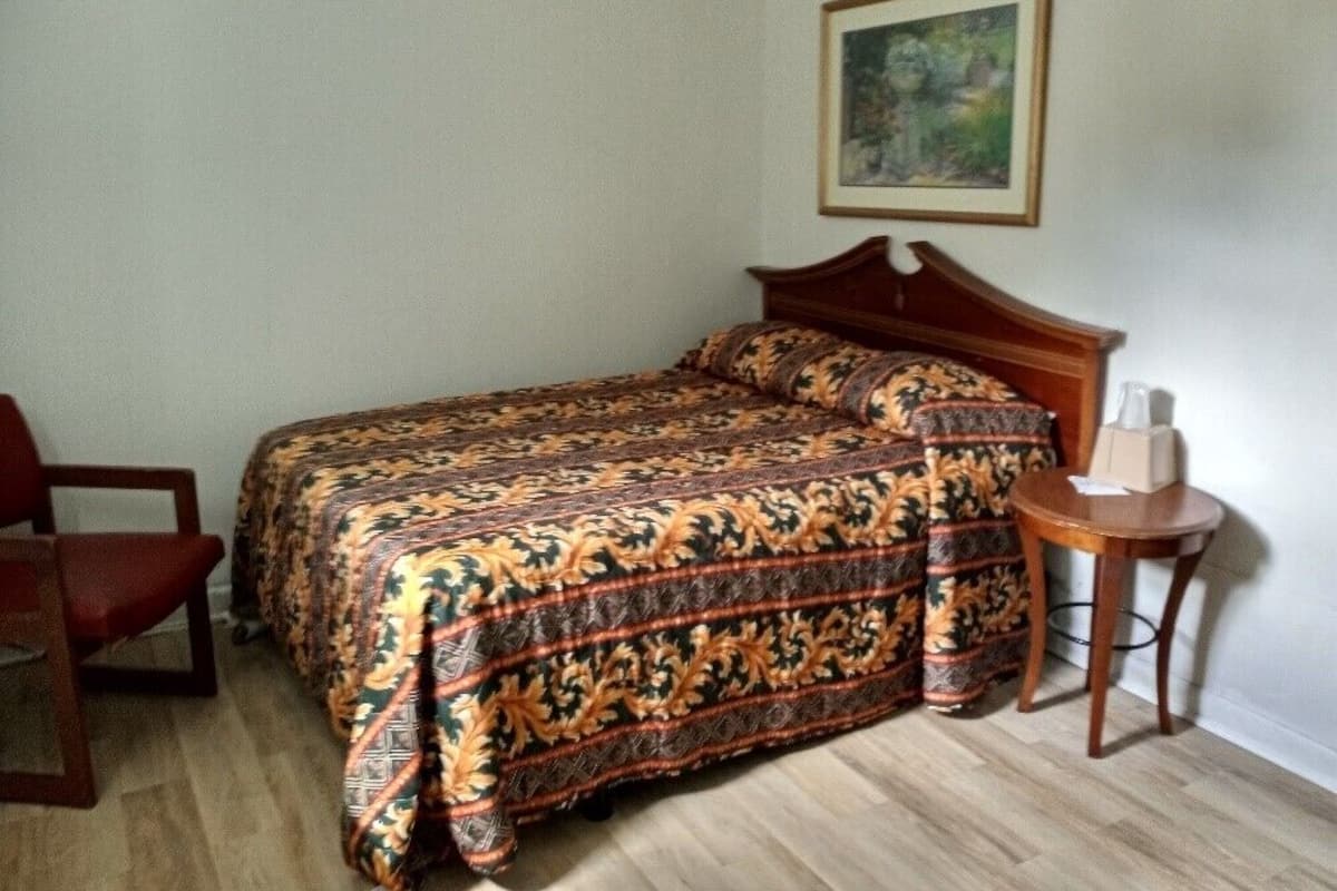 Um quarto com uma cama, uma cadeira, uma mesa pequena e um quadro na parede.