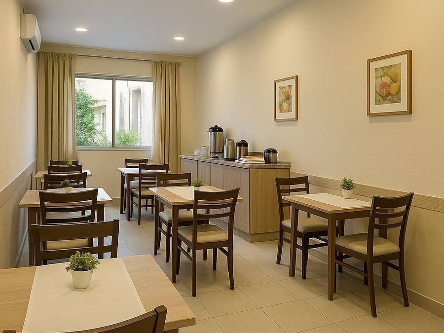 Uma área de refeições com várias mesas e cadeiras, uma cozinha compacta e uma janela com cortinas.