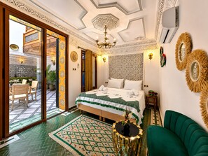 Quarto de hotel com uma cama, um sofá verde, um tapete estampado e vista para o pátio externo.