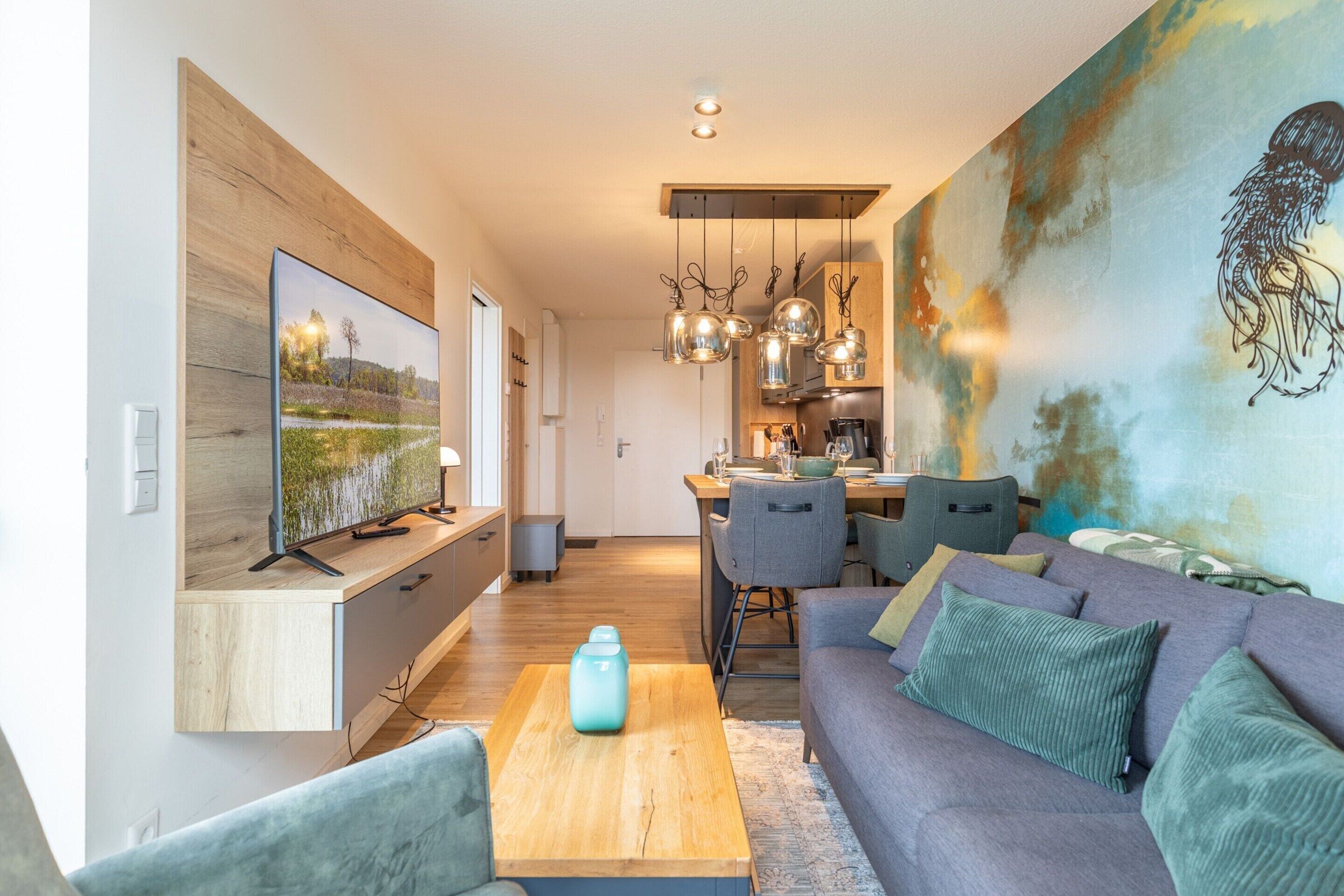 Uma sala de estar moderna com uma televisão de tela plana grande, um sofá cinza e uma mesa de centro de madeira.