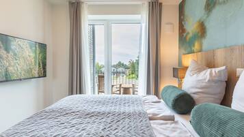 Quarto de hotel com uma cama grande, vista por uma porta de vidro e um quadro na parede.