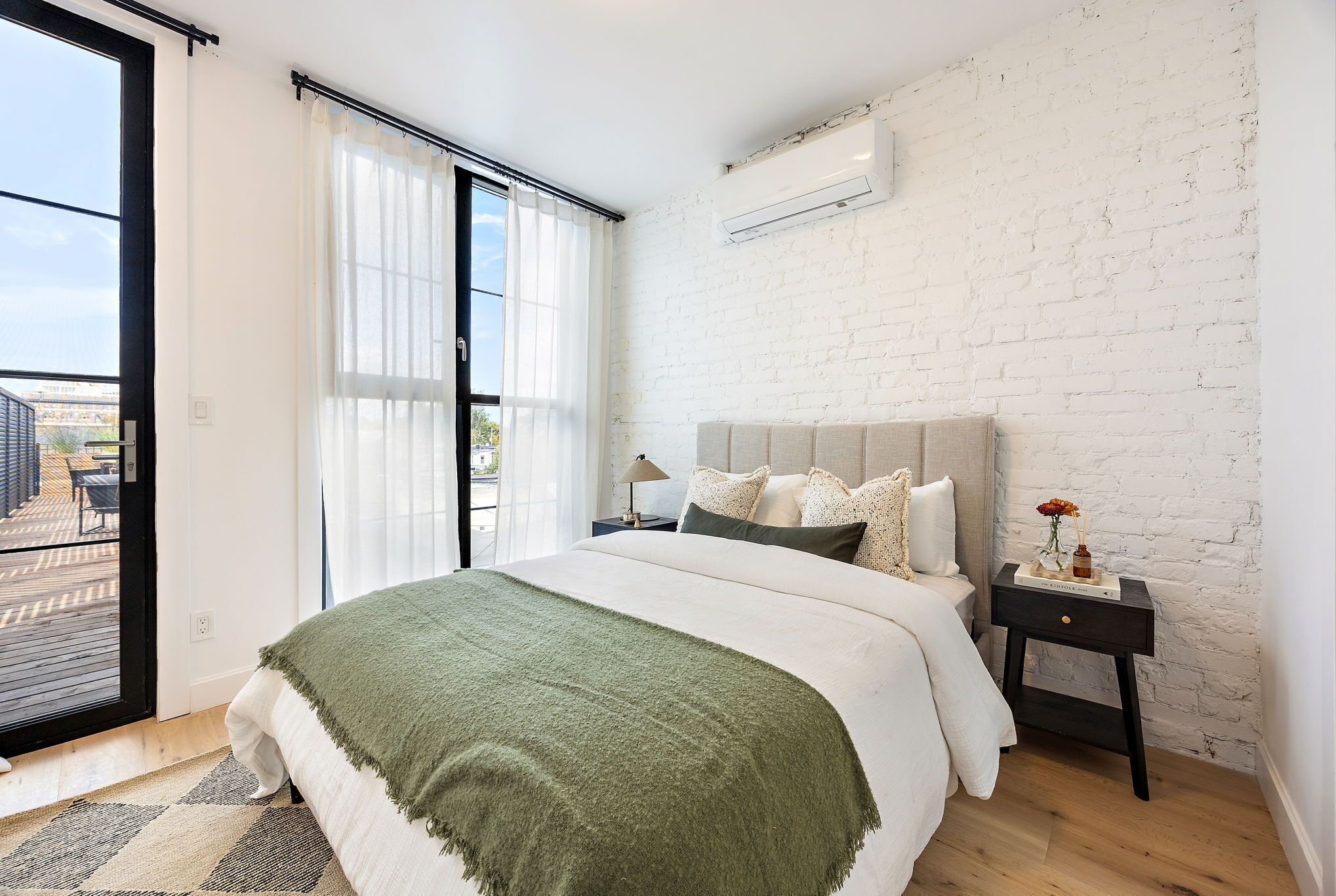 Quarto com uma cama grande, mesa de cabeceira, luminária e vista para área externa por uma porta deslizante.