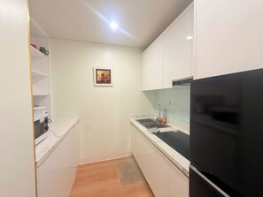 Uma cozinha compacta com armários brancos, geladeira preta e bancada pequena.