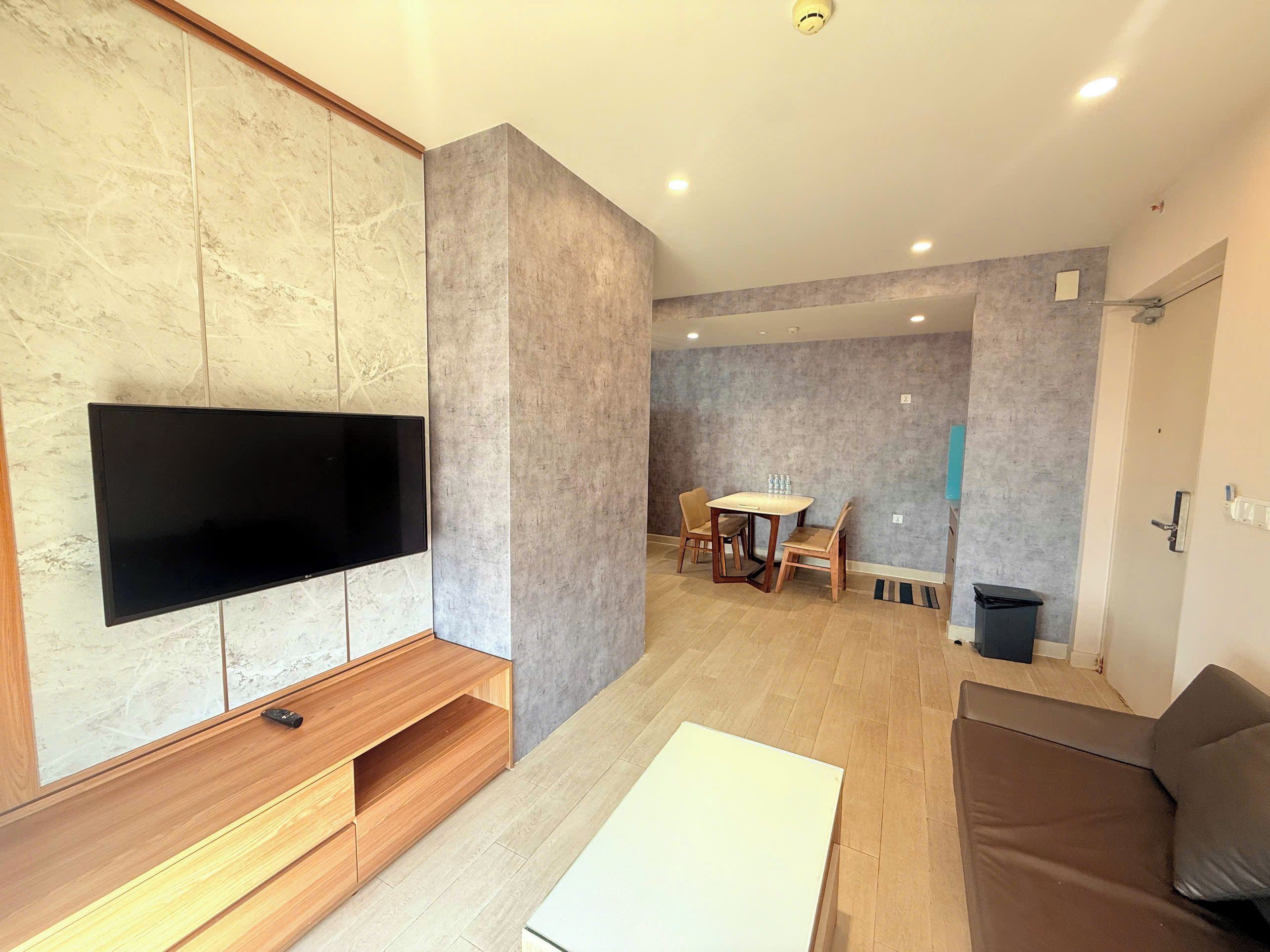 Uma sala de estar moderna com televisão de tela plana, móvel de entretenimento de madeira, um sofá e um espaço de jantar com mesa e cadeiras.