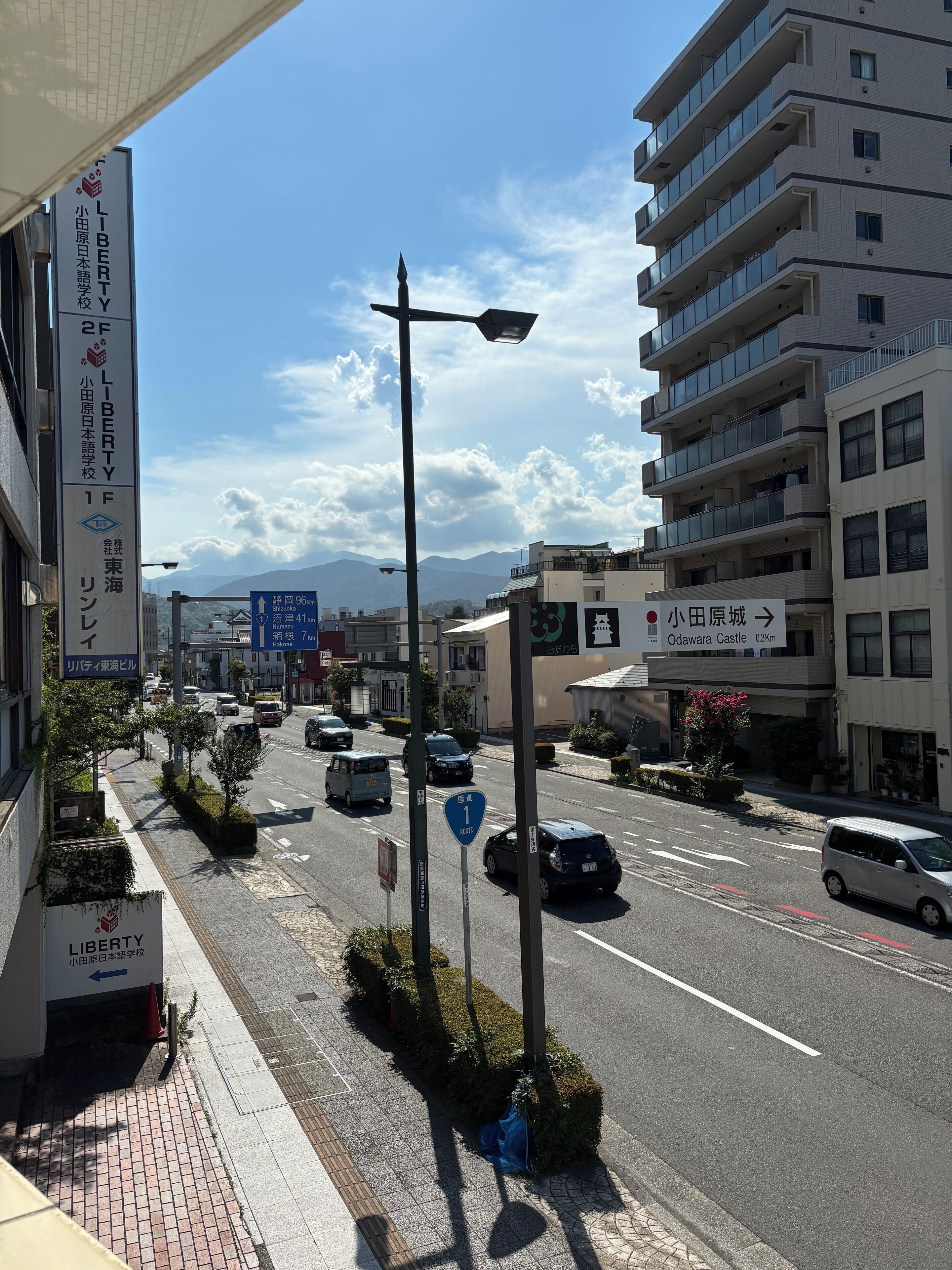 Vista da rua com um edifício identificado como 'Liberty' e uma placa indicando 'Castelo de Odawara, 0.3km'.