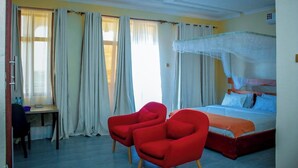 Um quarto com uma cama, uma escrivaninha e duas cadeiras vermelhas.