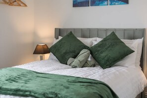 Cama bem arrumada com cabeceira cinza, duas almofadas verdes e um cobertor verde.
