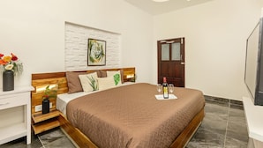 Um quarto moderno com cabeceira de madeira, uma cama grande, um criado-mudo branco com um vaso de flores, uma fotografia emoldurada de uma tigresa na parede e uma porta com painéis de vidro jateado.