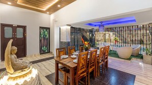 Uma sala de jantar com uma mesa e cadeiras de madeira, uma estátua de Buda e um painel decorativo.