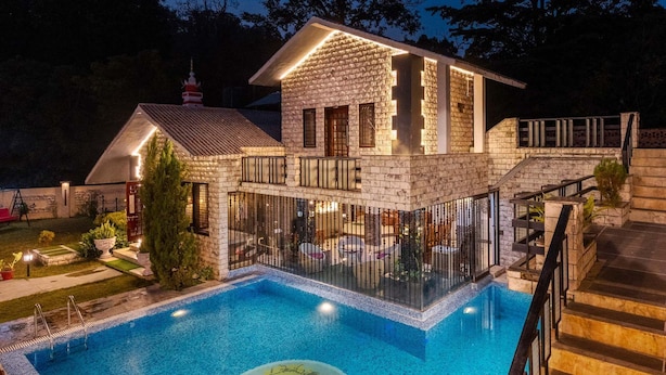 Uma casa de pedra de dois andares com piscina, área de estar ao ar livre e escadaria que dá acesso ao andar superior.
