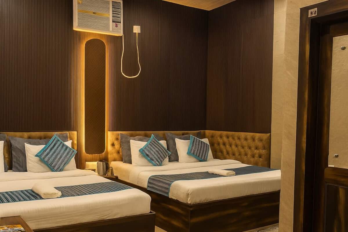 Quarto de hotel com duas camas, um ventilador de teto, aparelho de ar condicionado fixado na parede e uma porta com maçaneta.