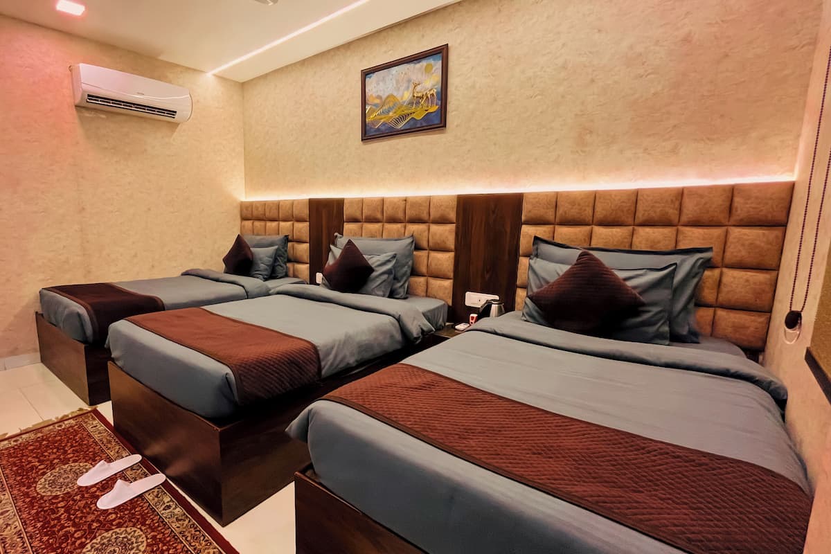 Quarto de hotel com três camas, um quadro grande na parede e um ar condicionado moderno.