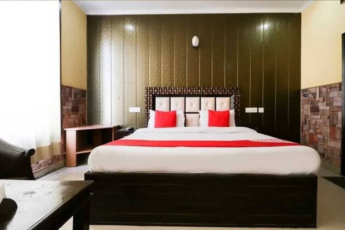 Quarto de hotel com uma cama grande, cabeceira com padrão decorativo e almofada vermelha.