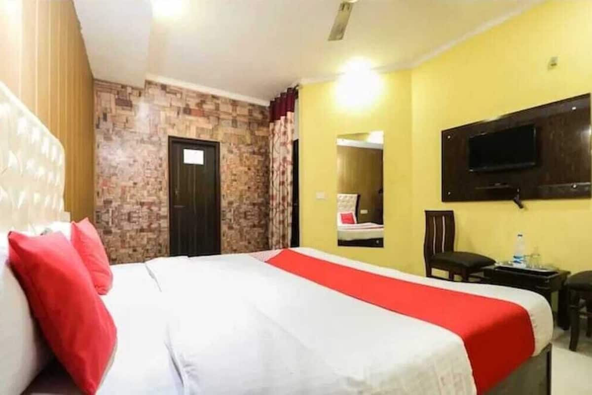 Quarto de hotel com cama, televisão fixada na parede, mesinha e uma cadeira.
