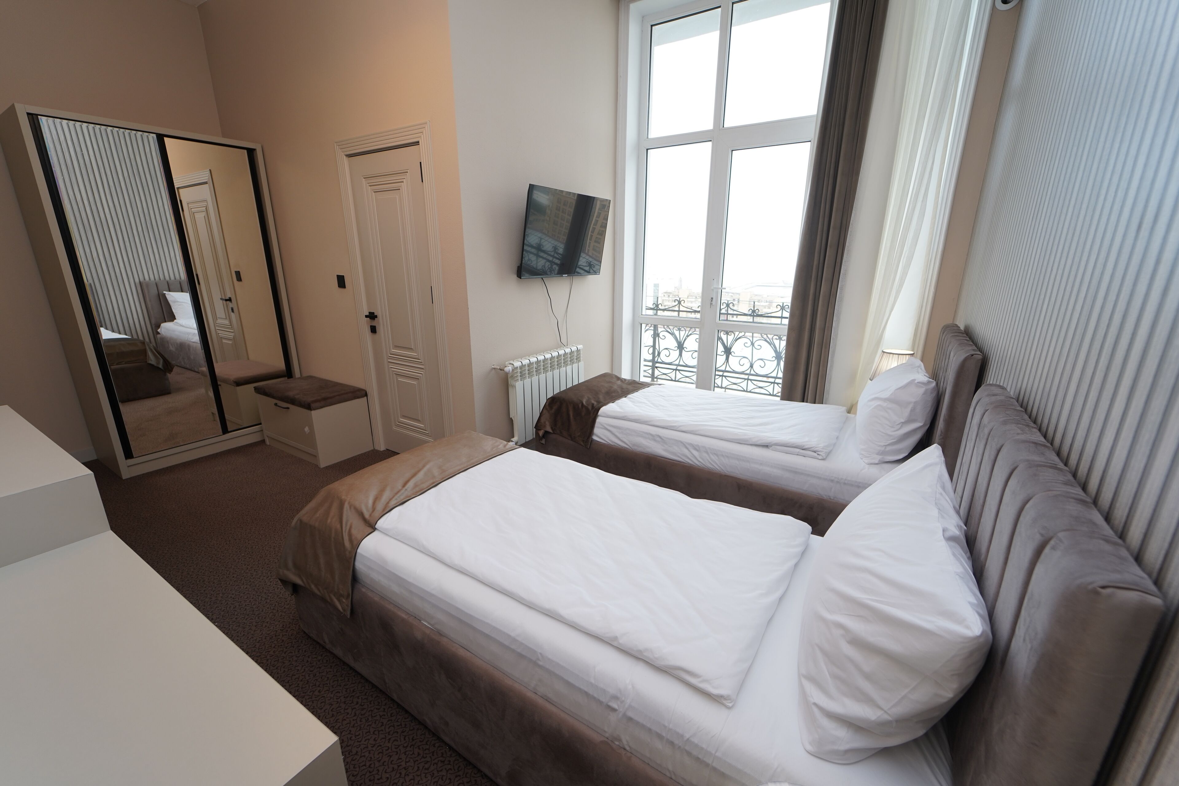 Quarto de hotel com duas camas, televisão, janela com vista, radiador e guarda-roupa.