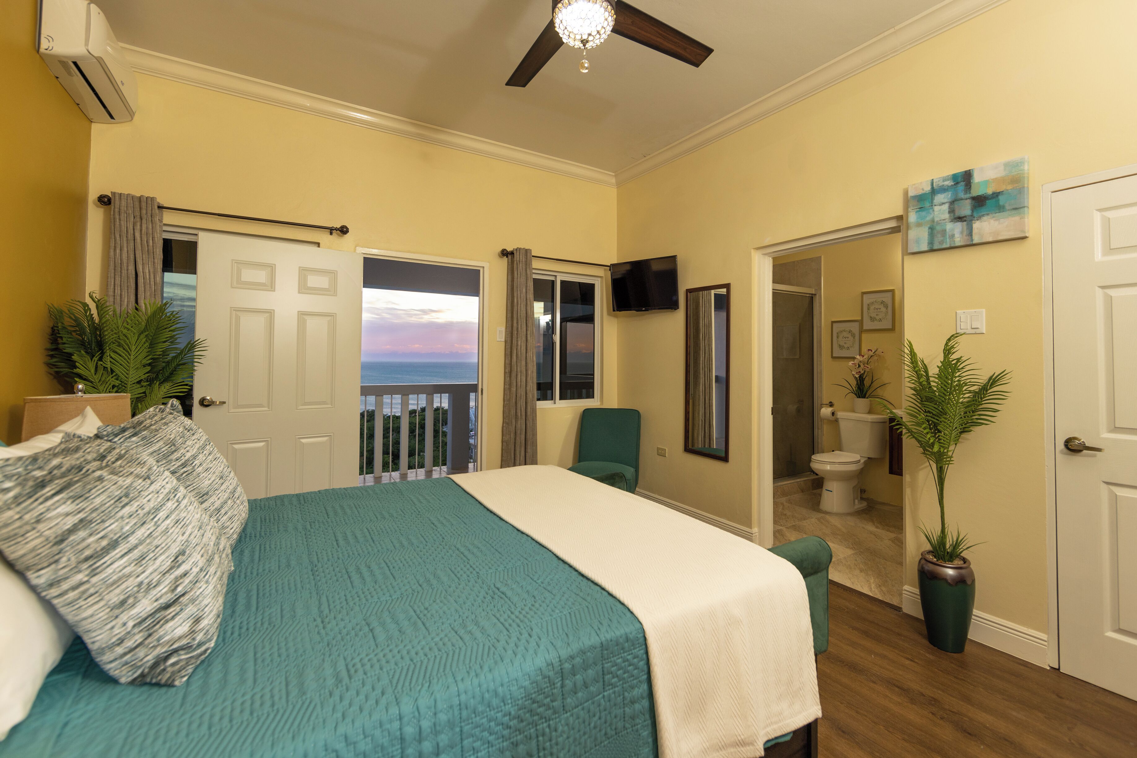 Quarto com cama, ventoinha no teto, televisão e vista para o oceano.