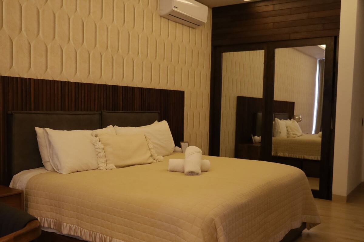 Cama bem arrumada com cabeceira, mesa de cabeceira e ar-condicionado fixado na parede.