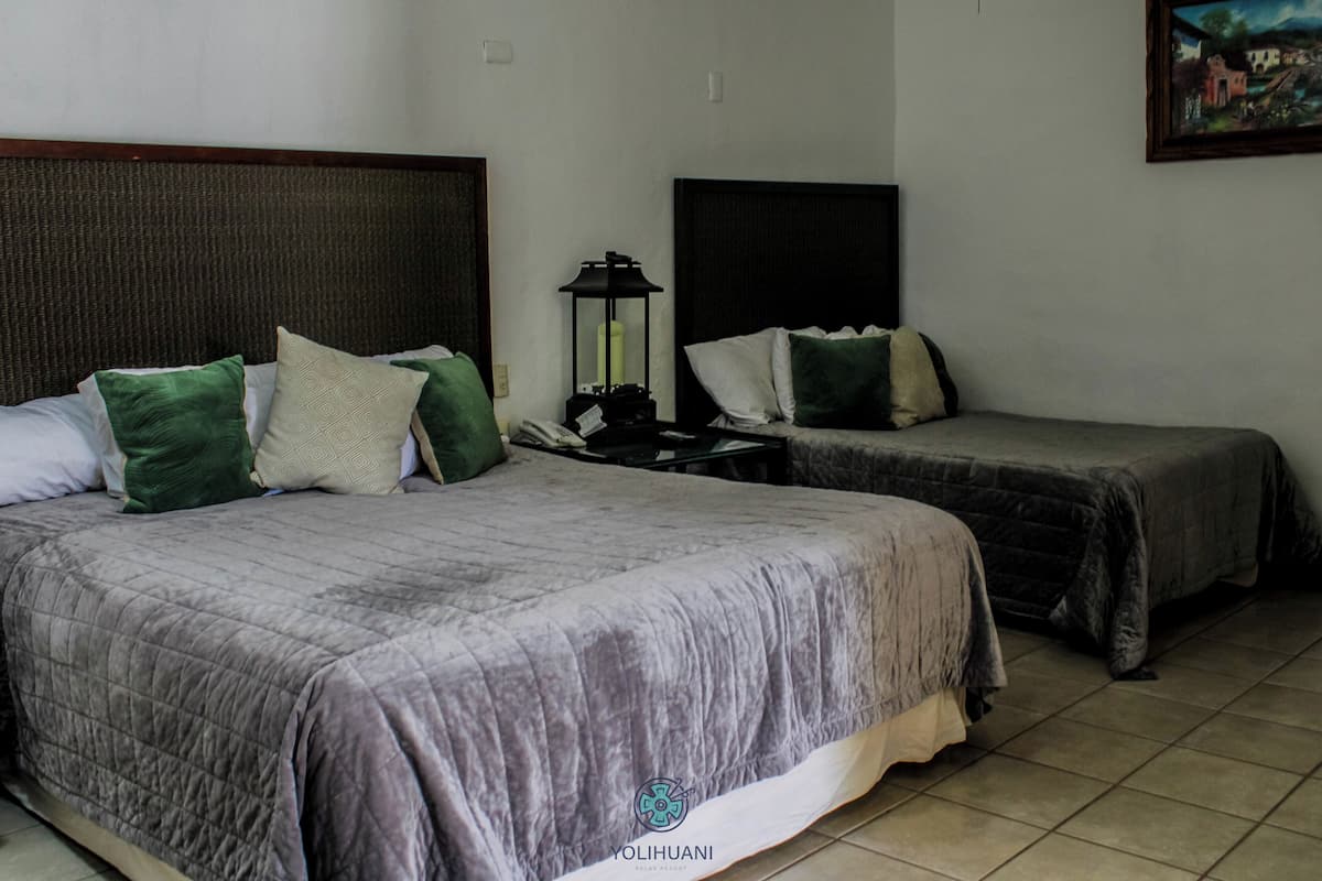 Quarto de hotel com duas camas, uma mesa de cabeceira, um abajur e um quadro na parede.