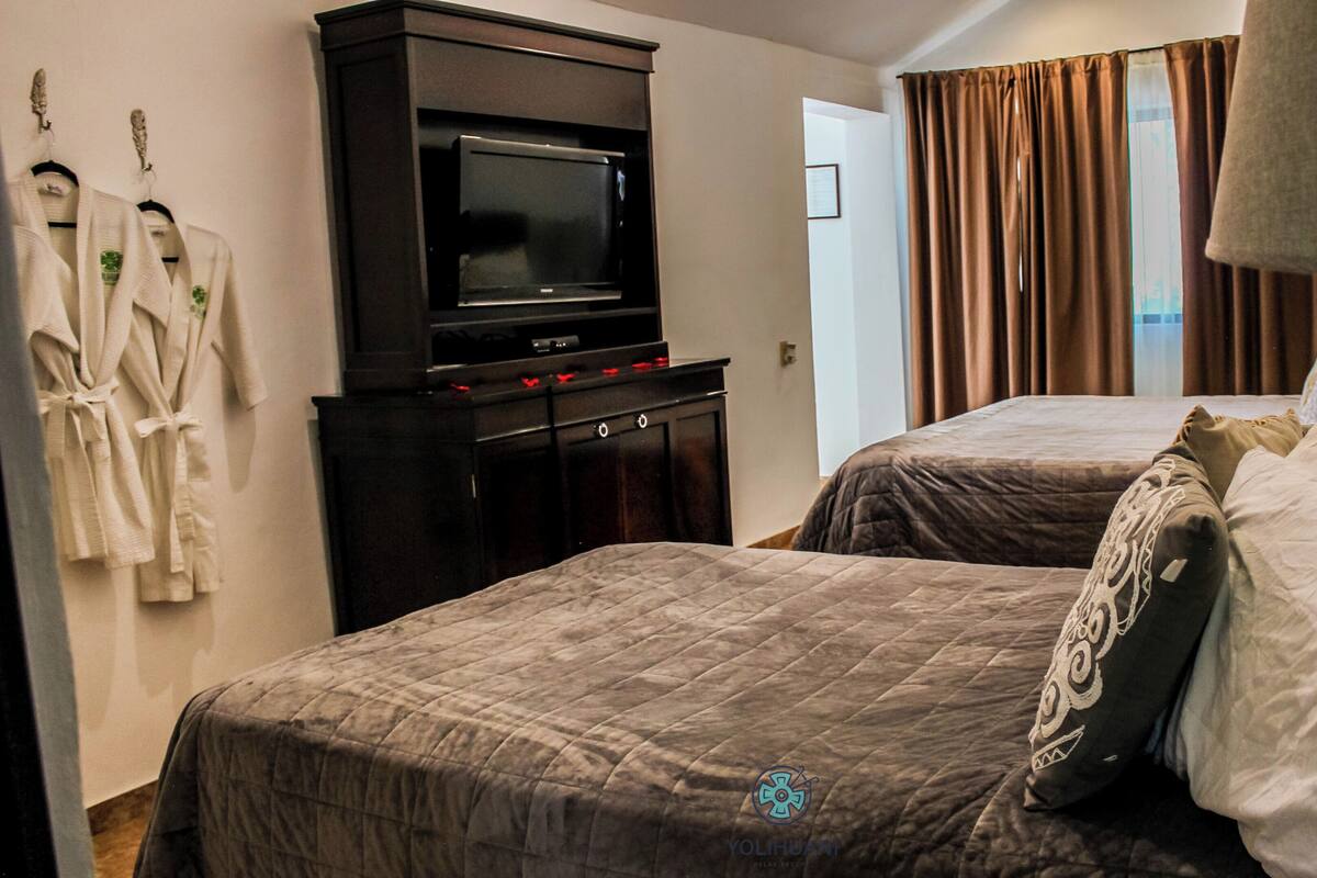 Quarto de hotel com duas camas, uma televisão e roupões pendurados na parede.