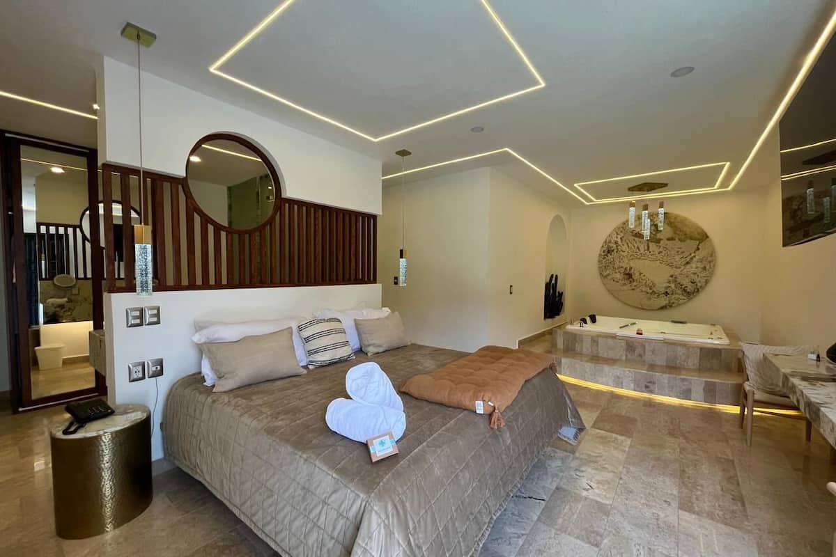 Quarto moderno com cama grande, espelho redondo, cabeceira de madeira, banheira e piso de pedra.
