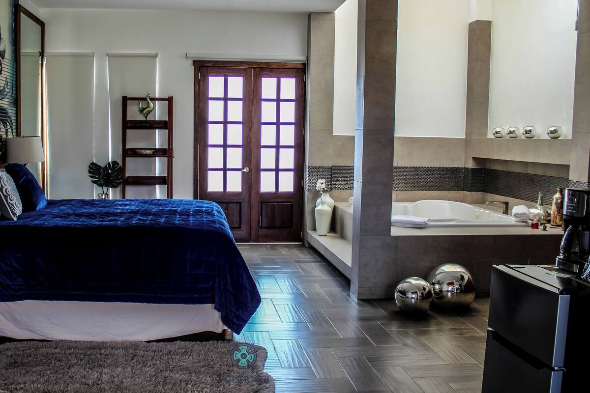 Quarto com uma cama grande, porta de madeira, banheiro com banheira e uma máquina de café.