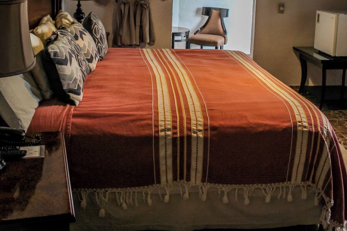 Quarto de hotel com cama grande, teto de madeira, luminária pendente e vista para o exterior.