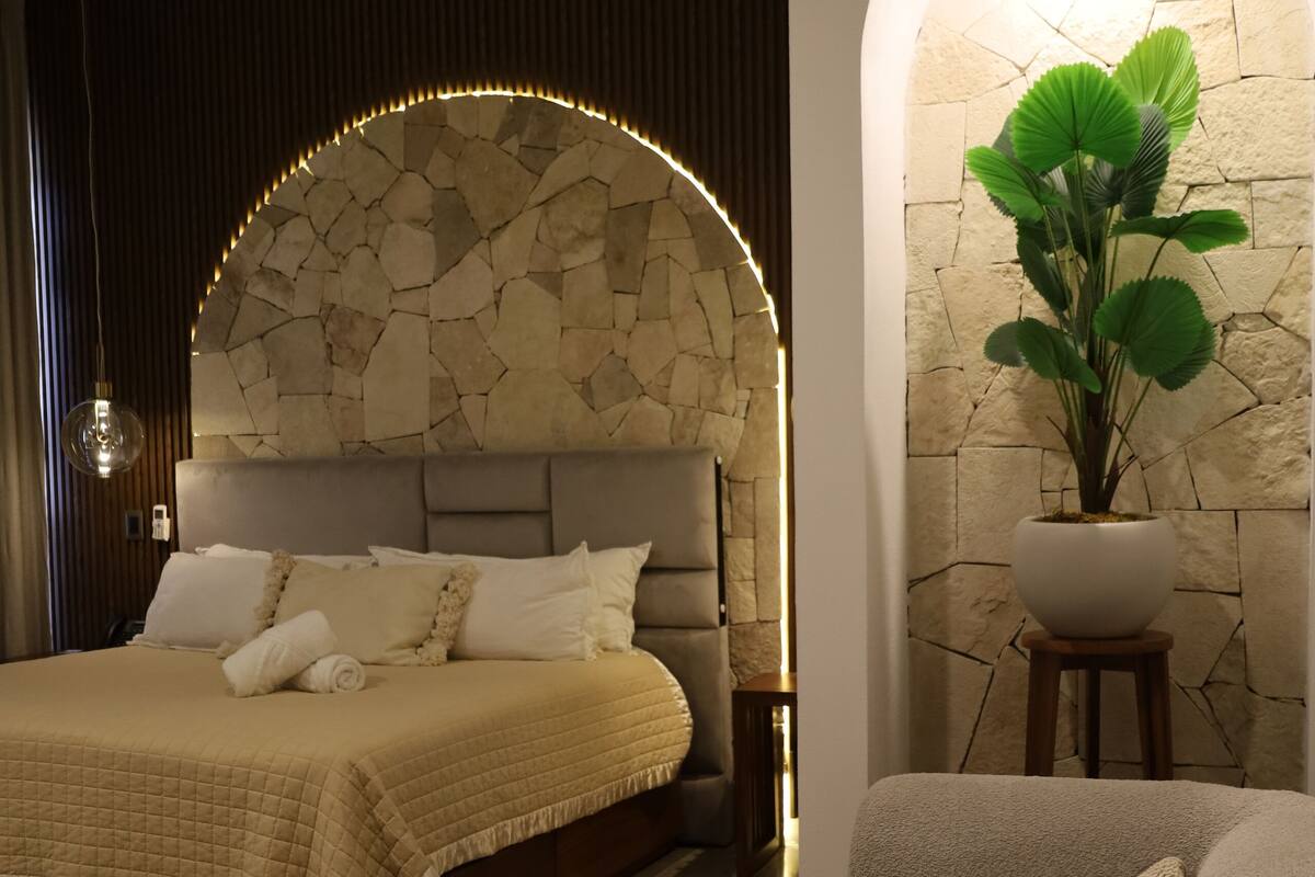 Quarto moderno com uma cama grande, um sofá, um vaso de planta e uma parede de pedra.