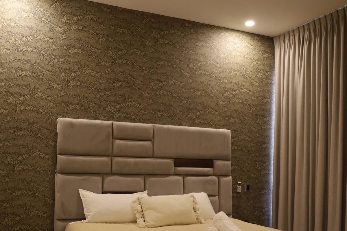 Quarto moderno com uma cama grande, cabeceira e parede texturizada.