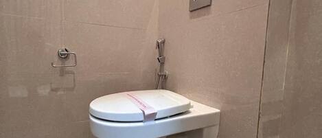 Um banheiro moderno com vaso sanitário suspenso, área de chuveiro e uma pequena prateleira sobre o vaso.