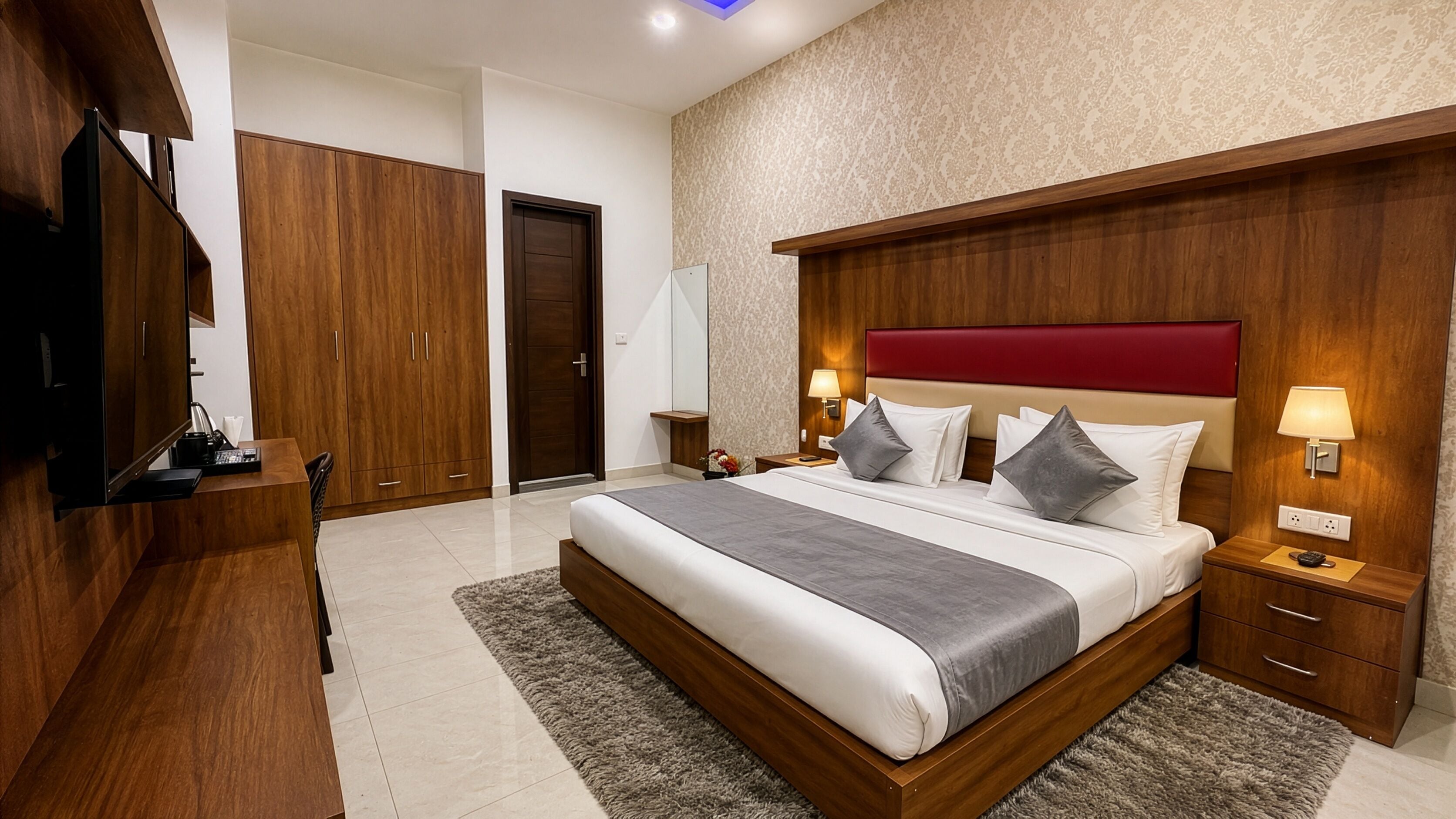 Quarto de hotel com cama grande, guarda-roupa de madeira e secretária com computador.